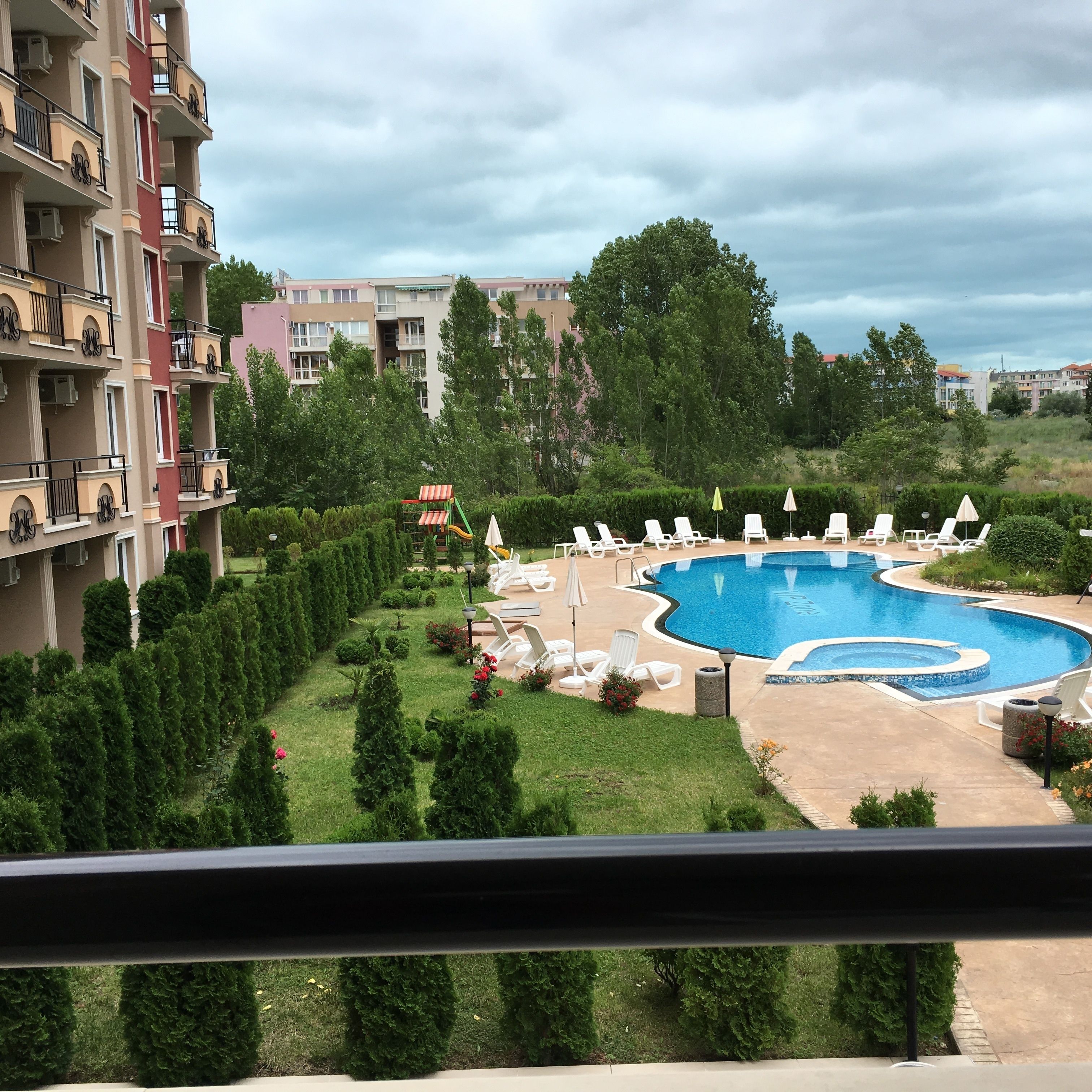 Edifício residencial com varandas, piscina e vegetação ao redor.