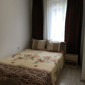 Quarto com cama, mesa de cabeceira, janela com cortinas e tomada na parede.