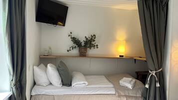 Quarto de hotel com cama, televisão na parede, prateleira com uma planta e abajur.