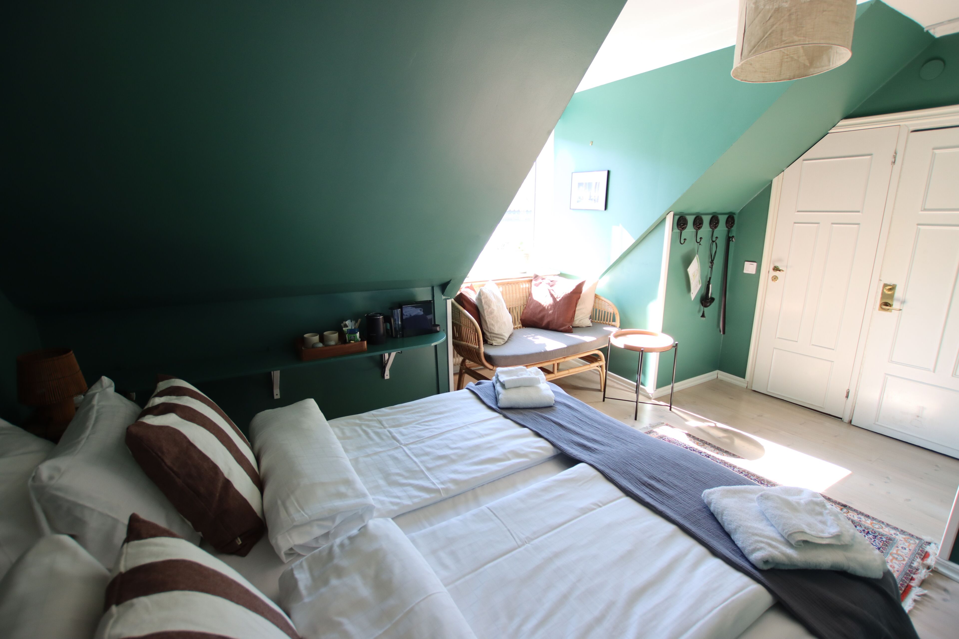 Quarto com cama, almofadas, uma cadeira, uma mesinha e um guarda-roupa.