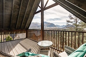 Um deck de madeira com uma mesa redonda e assentos, com vista para uma paisagem montanhosa.