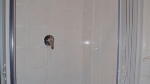 Um banheiro com paredes revestidas de azulejos brancos, um chuveiro com torneira cromada e uma pia branca.