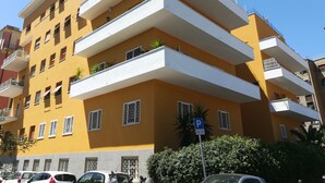 Um edifício amarelo de vários andares, com varandas, um sinal de estacionamento e um céu azul límpido.