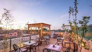 Terraço no telhado com mesas, cadeiras, pérgula e plantas em vasos.