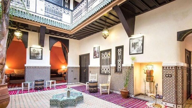 Um interior tradicional marroquino com um pátio, azulejos estampados e uma área de estar central.