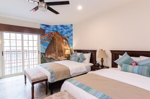 Quarto de hotel com duas camas, um mural de um edifício, um ventilador de teto e vista através de uma porta de correr.