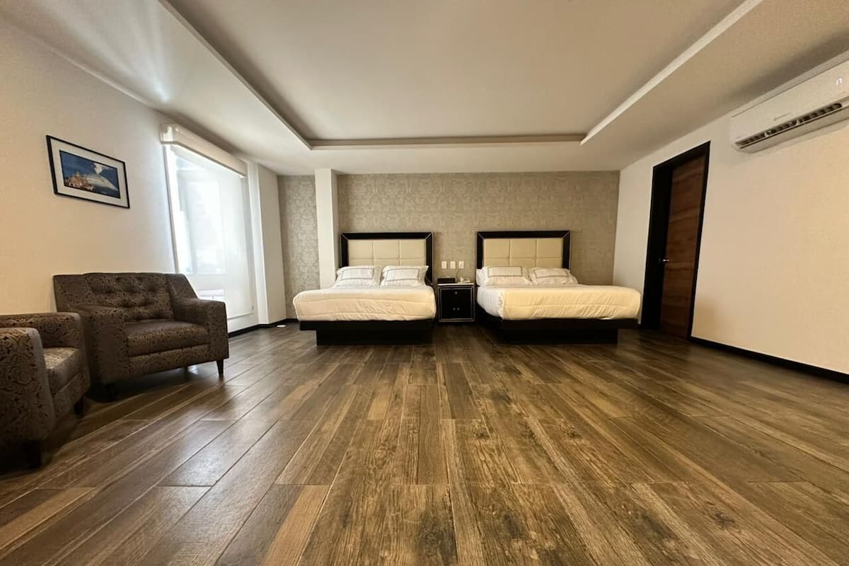 Quarto de hotel com duas camas, um sofá, uma janela grande e um quadro na parede.