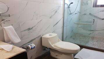 Um banheiro com vaso sanitário, box de chuveiro em vidro, parede com azulejos de mármore, porta-toalhas e dispensador de papel higiênico.
