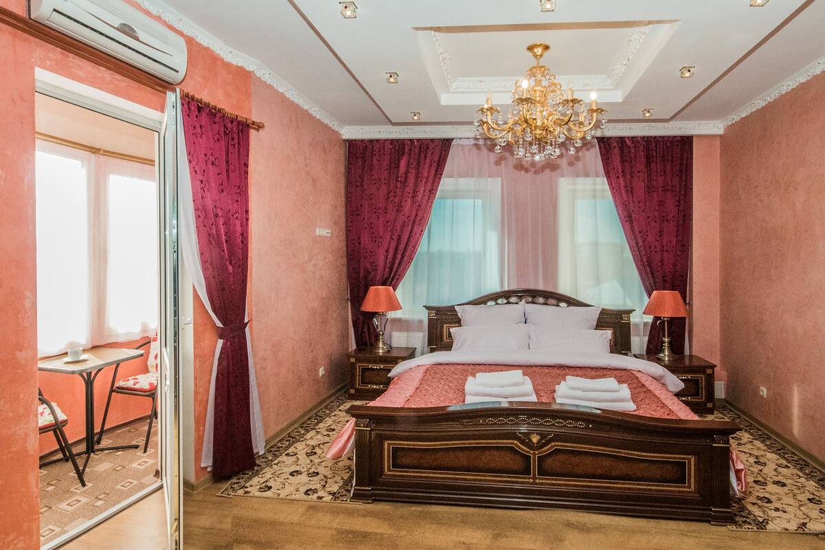 Quarto com uma cama grande, duas luminárias de cabeceira, um lustre e vista para uma varanda.