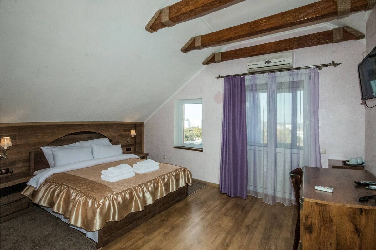 Quarto com cama de madeira, mesa de cabeceira, janela com cortinas e televisão na parede.