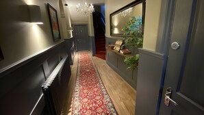 Um corredor com carpete estampado em vermelho, um radiador, um candelabro e uma porta com fechadura.