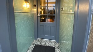 Um corredor estreito com paredes em azulejos verdes, chão estampado e uma porta com janela.