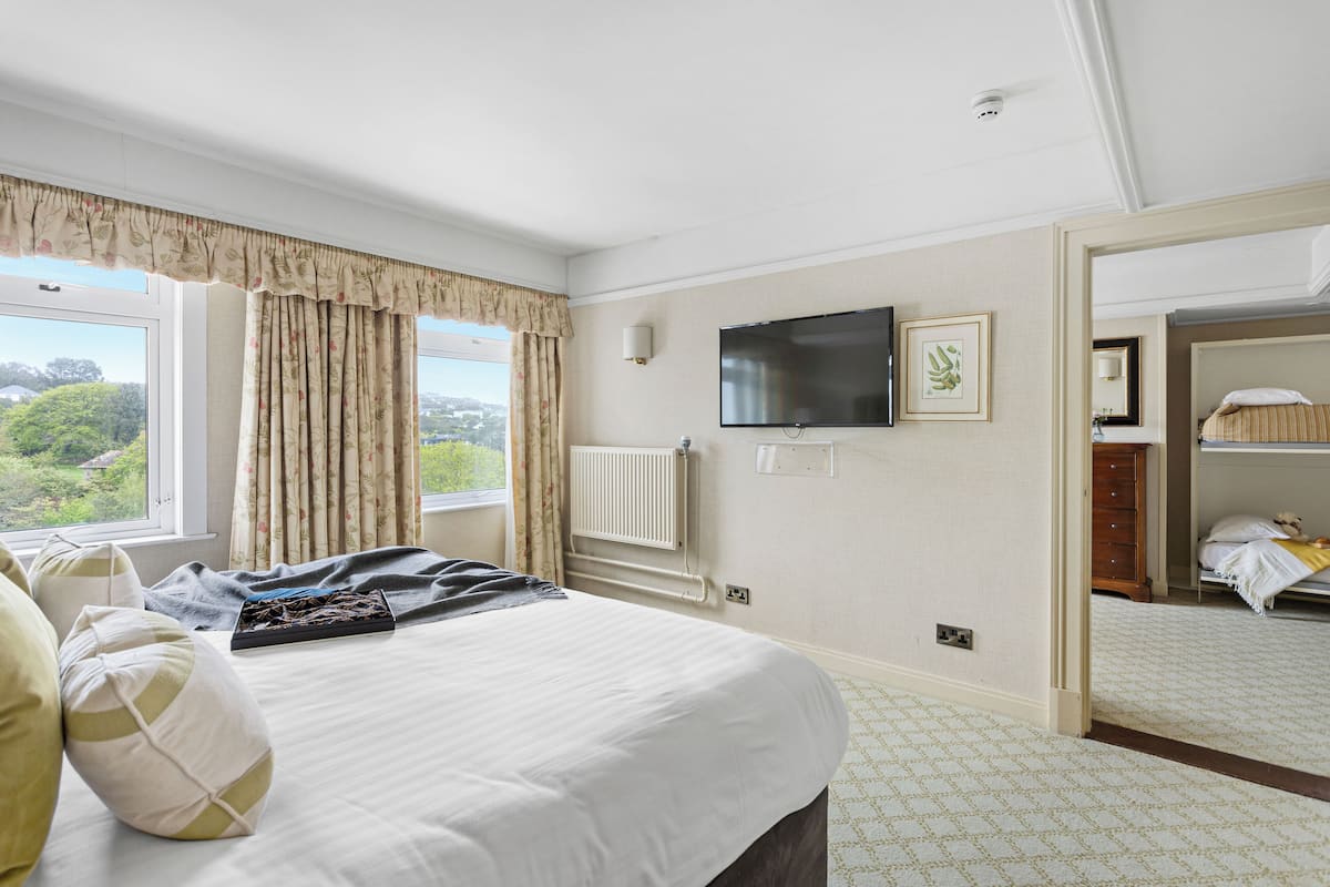 Quarto de hotel com uma cama grande, televisão na parede e vista para o exterior pela janela.