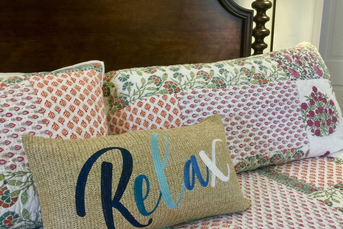 Cama com roupa de cama estampada com flores e almofada com a palavra 'Relax'.
