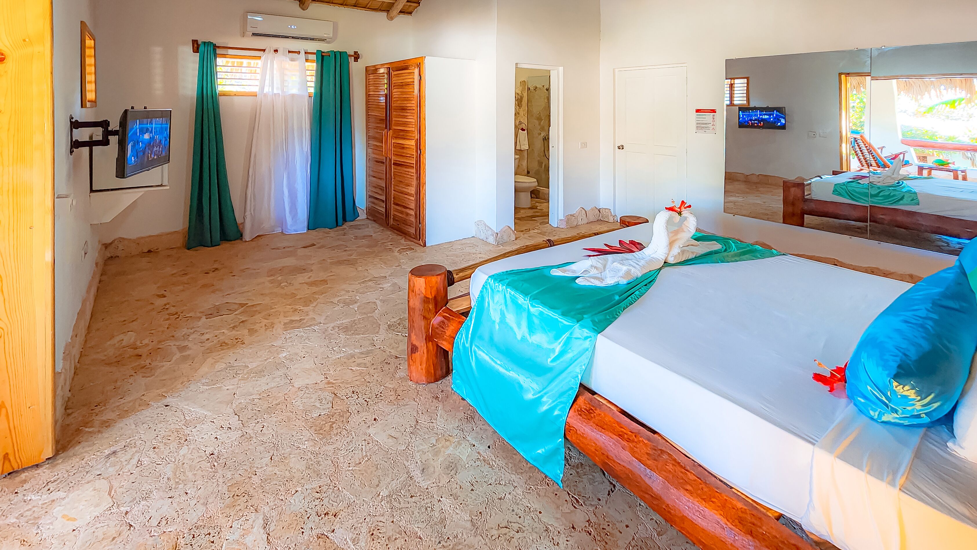 Quarto com cama, um banco de madeira, televisão e área de chuveiro.