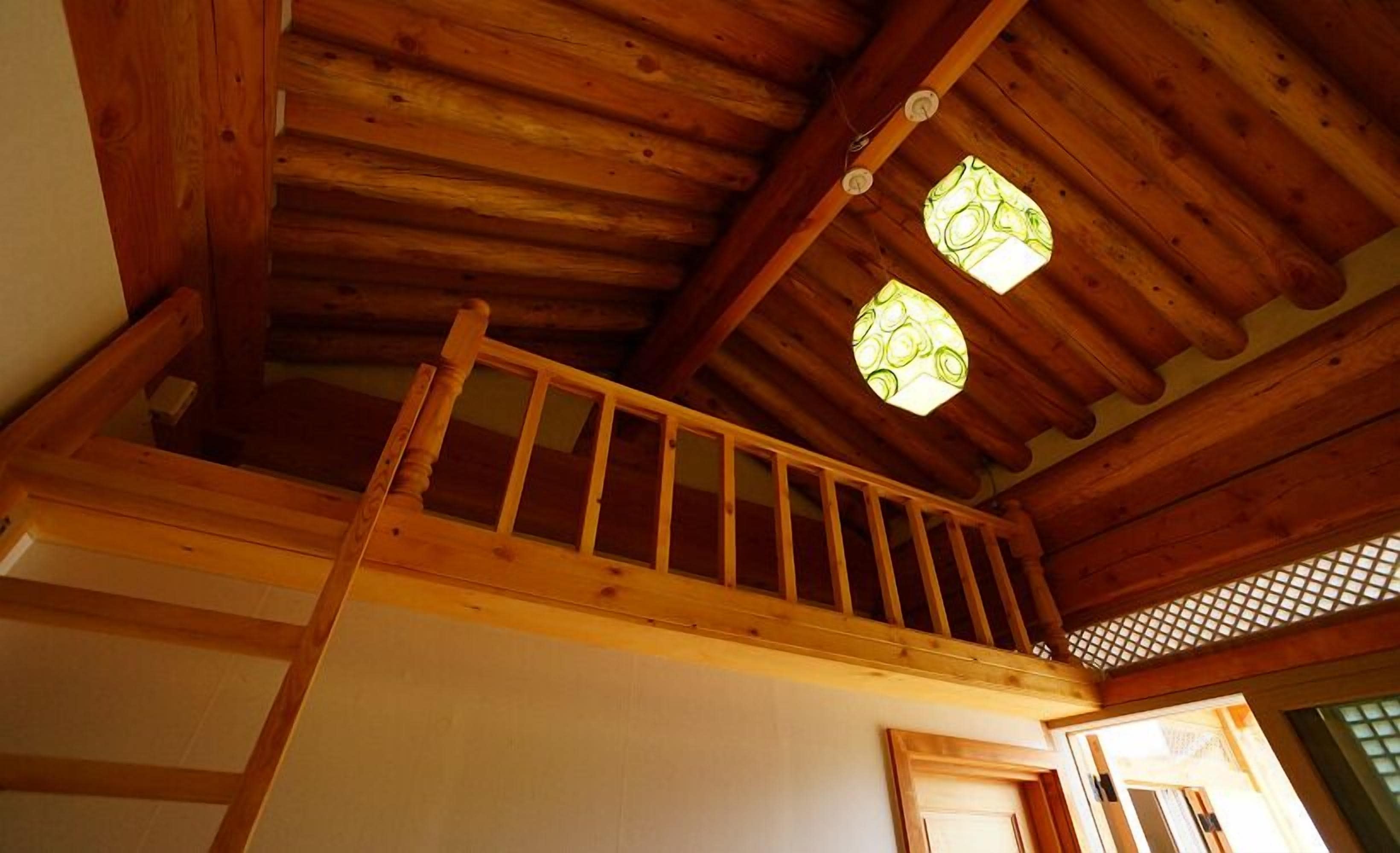 Interior de madeira com teto inclinado, vigas de madeira e escada visível.