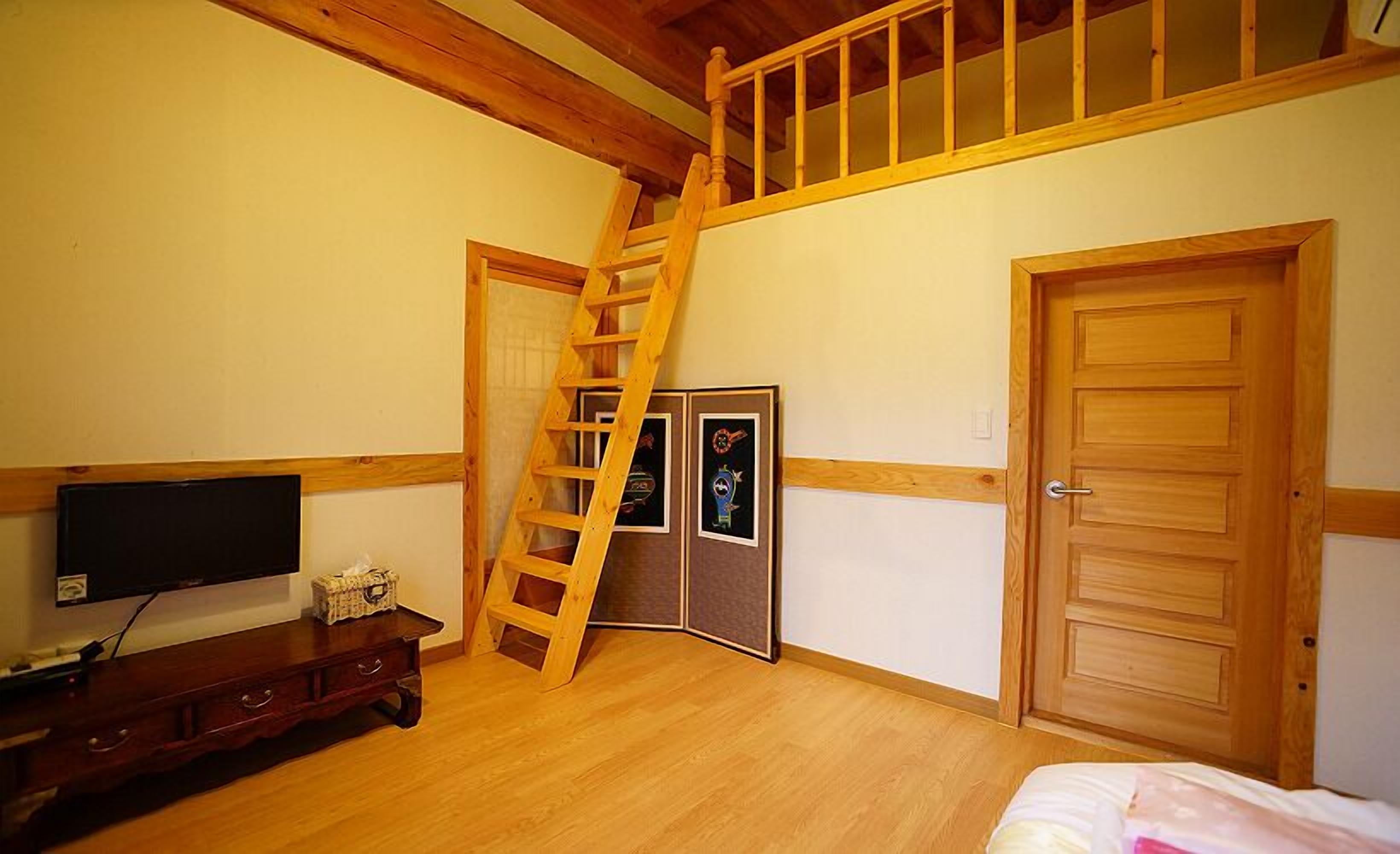 Quarto com escada de madeira para um mezanino, televisão em uma cômoda e duas portas.