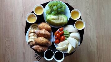 Uma bandeja de refeição com diversos alimentos, incluindo uvas, melão, croissants, tomates cereja e dois tipos de molhos.