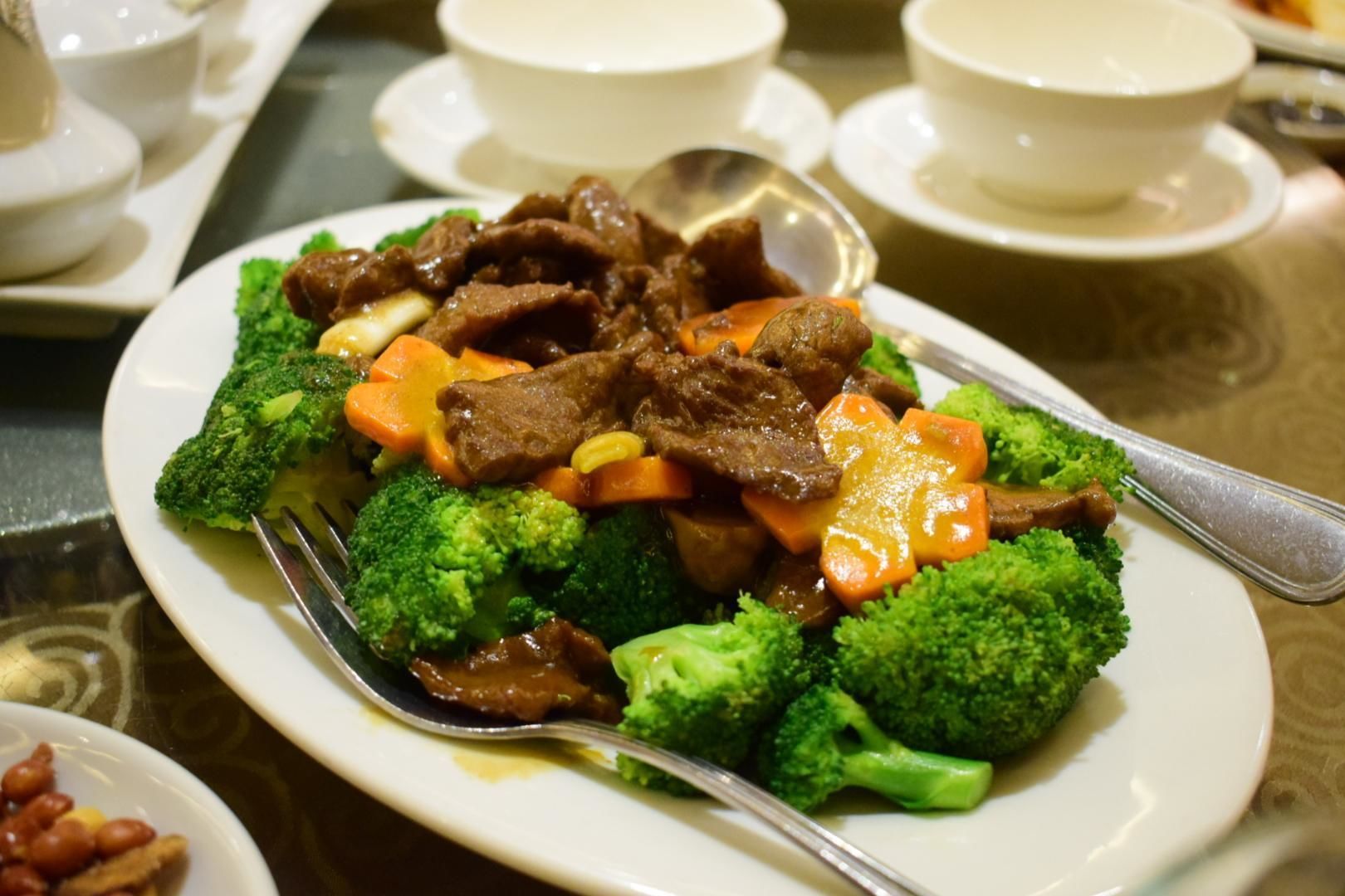 Prato de carne e legumes, incluindo brócolis e cenouras, servido em um prato branco com uma colher.