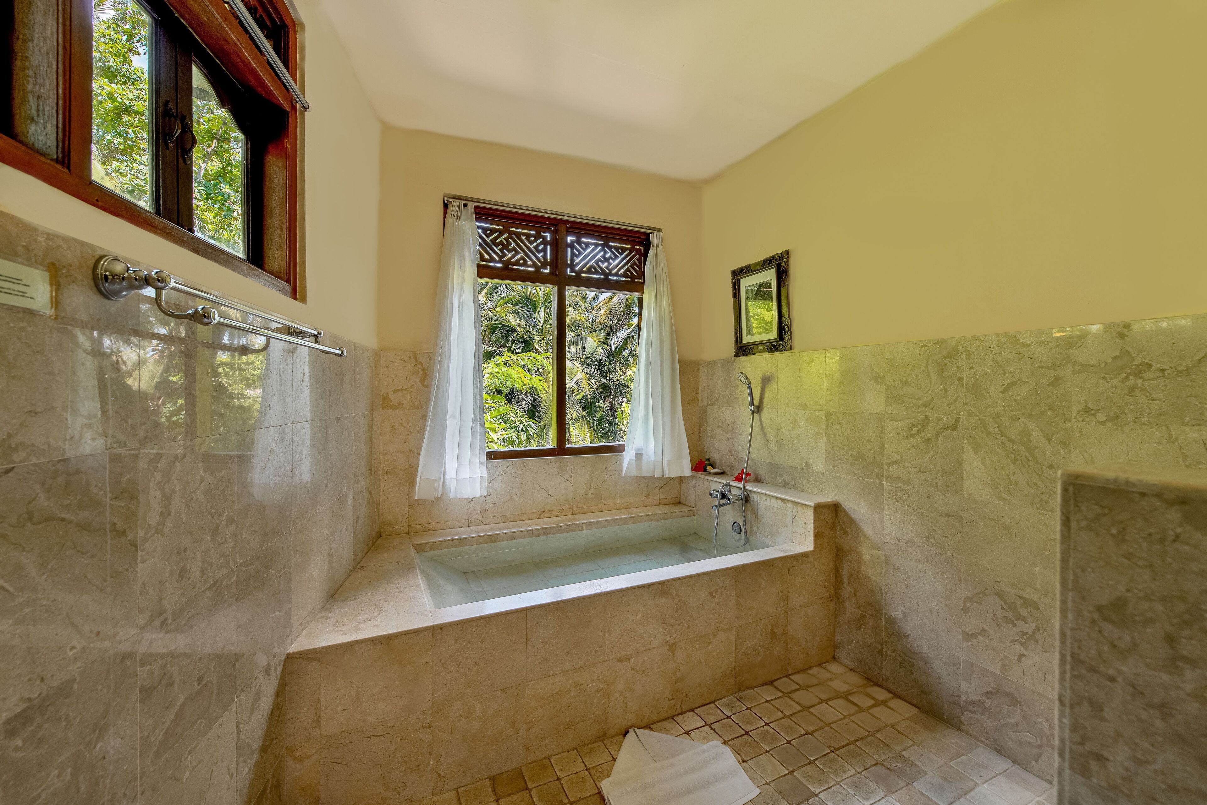 Uma casa de banho com banheira, janela com cortinas, área de chuveiro e parede de mármore.
