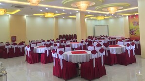 Uma sala de banquetes com mesas redondas, cadeiras e um palco.