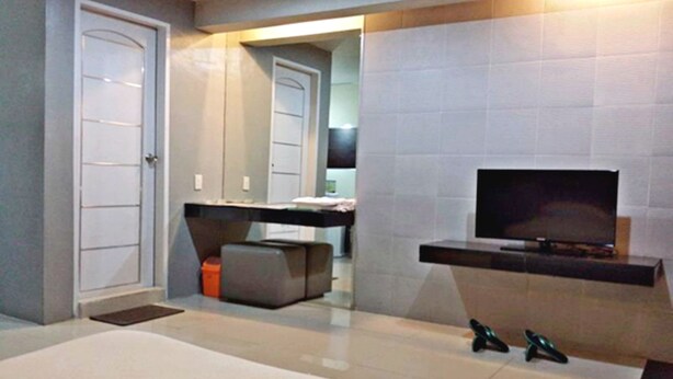 Quarto de hotel moderno com televisão de tela plana, um pequeno espaço de estar e banheiro visível por uma porta aberta.