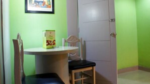 Quarto com parede verde, porta branca, mesa redonda com uma cadeira e um quadro na parede.