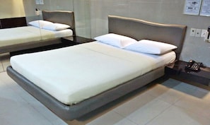Quarto de hotel moderno com uma cama grande, uma mesinha de cabeceira e um espelho.