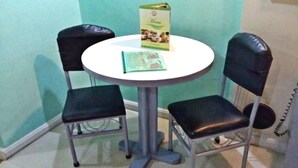 Uma pequena mesa redonda com tampo branco, rodeada por duas cadeiras de couro preto. Uma caixa verde com a palavra 'Menu' está colocada sobre a mesa.