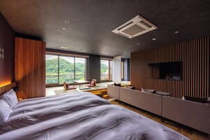 Quarto de hotel moderno com uma cama grande, um sofá, uma televisão e vista para uma montanha.