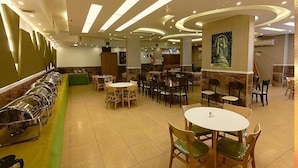 Um saguão de hotel com área de buffet, várias mesas de jantar e uma grande pintura na parede.