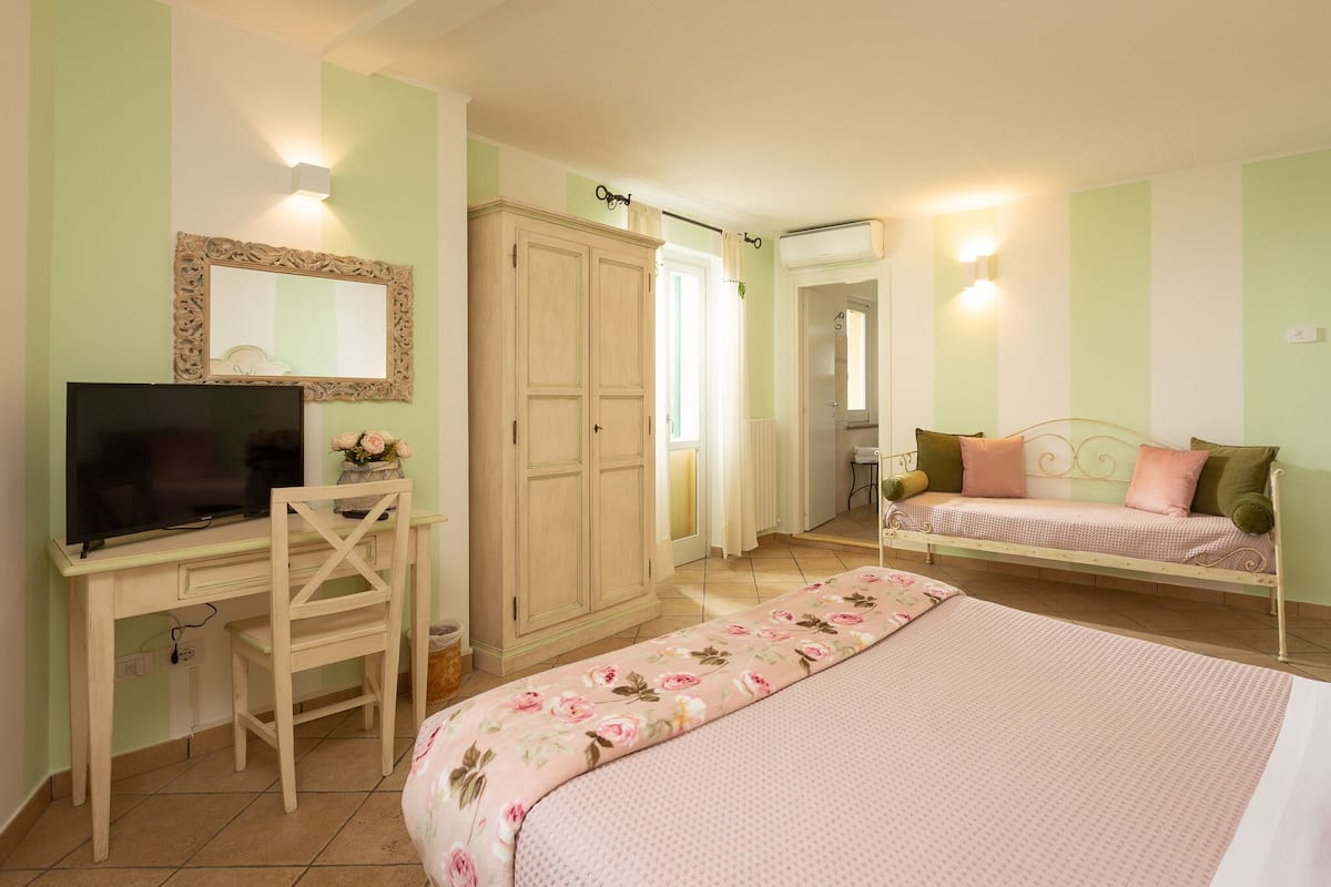 Quarto com cama, escrivaninha com televisão, guarda-roupa e sofá.
