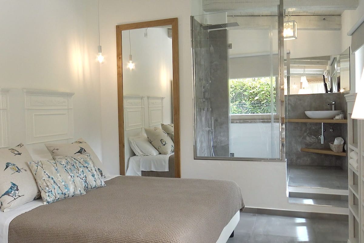 Quarto com cama, um espelho grande e banheiro visível por uma porta aberta.