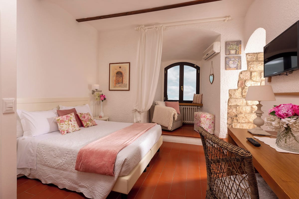 Quarto com cama, escrivaninha, cadeira, televisão e janela com vista.