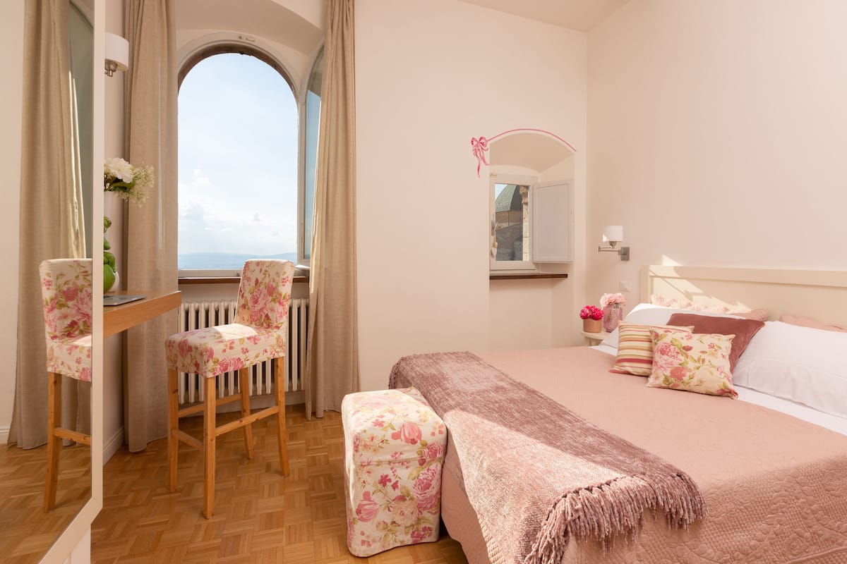 Quarto com cama, cadeira, escrivaninha e janela.