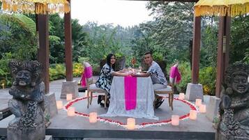 Um casal sentado à mesa com toalha rendada branca, rodeado por velas e a mensagem 'I LOVE YOU' no chão.