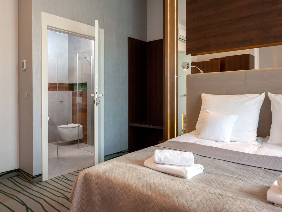 Quarto de hotel com uma cama, zona de chuveiro e cabeceira de madeira.