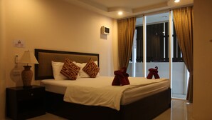 Quarto de hotel com uma cama grande, mesa de cabeceira com abajur e vista para o exterior por uma porta de correr.