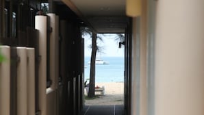 Corredor que dá para uma praia, com um banco e um barco ao longe.