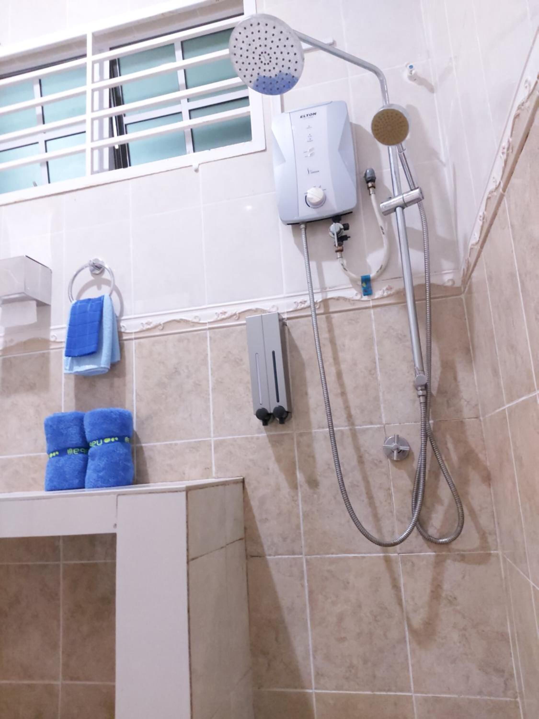 Casa de banho com chuveiro, um porta-toalhas com toalhas azuis e um aquecedor de água.