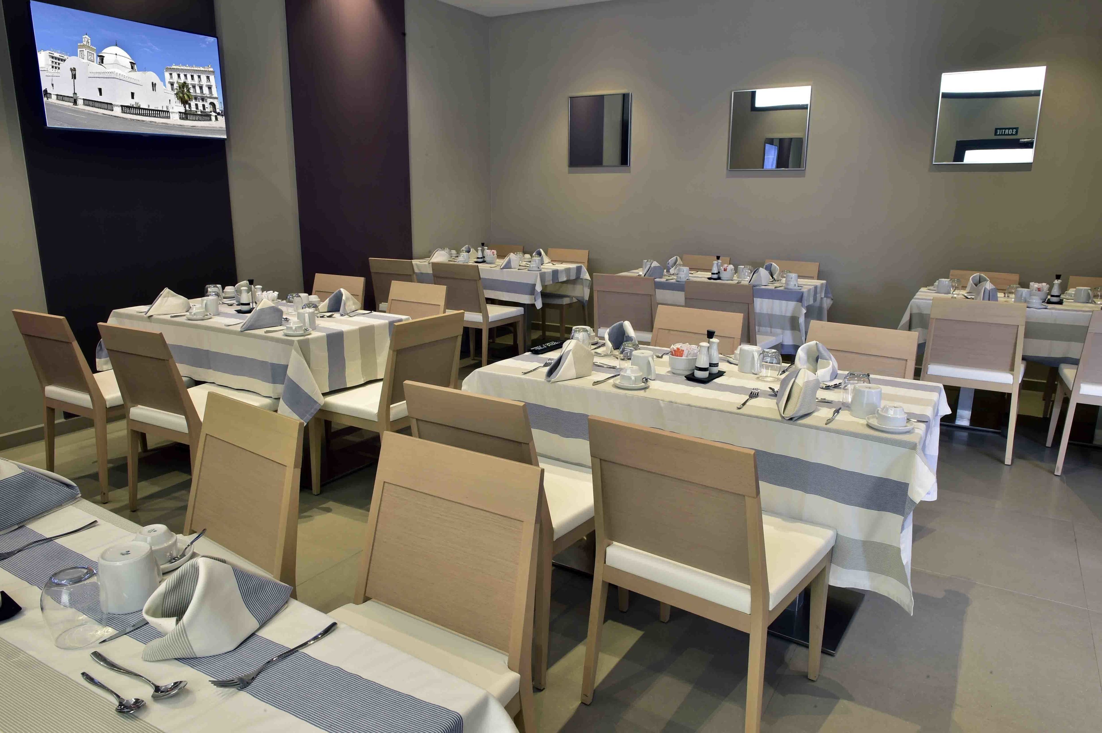 Uma sala de jantar com várias mesas montadas para hóspedes, com louças e cadeiras.