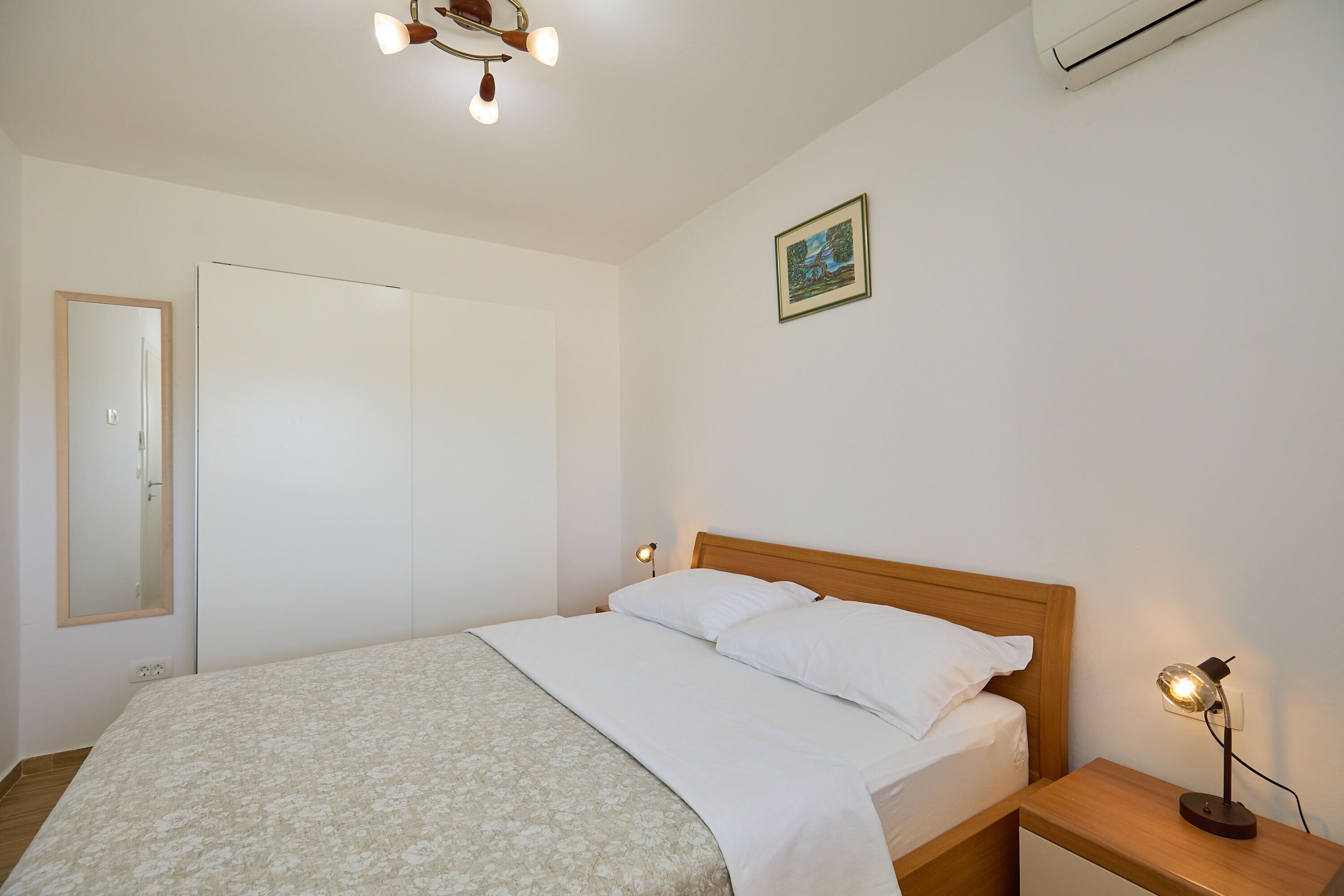 Quarto com cama, mesa de cabeceira, abajur, guarda-roupa e um quadro na parede.
