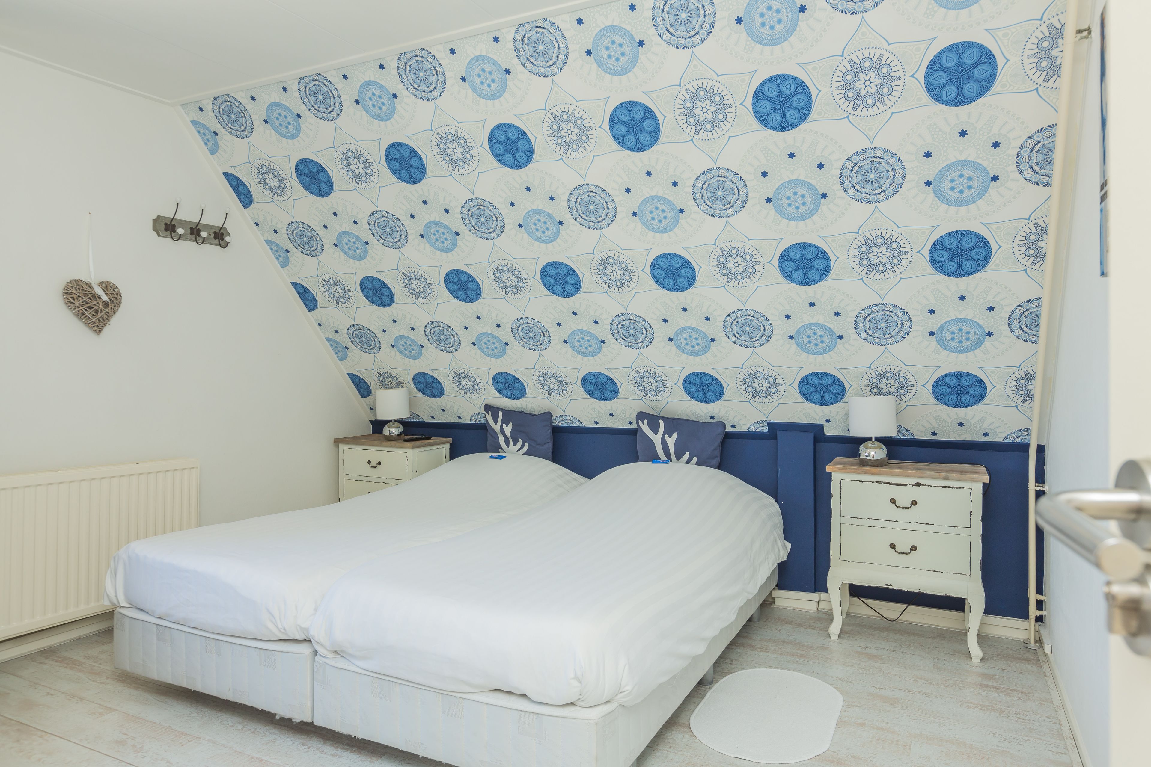Quarto com cama, duas mesas de cabeceira, cômoda e parede estampada.