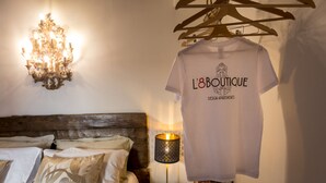 Quarto com cabeceira de madeira, lustre, camiseta branca pendurada com texto, luminária e pequena mesa com um livro e uma maçã.