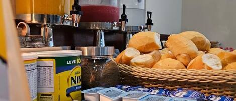 Um buffet de café da manhã com diversos alimentos, incluindo pães, sucos e potes de iogurte.