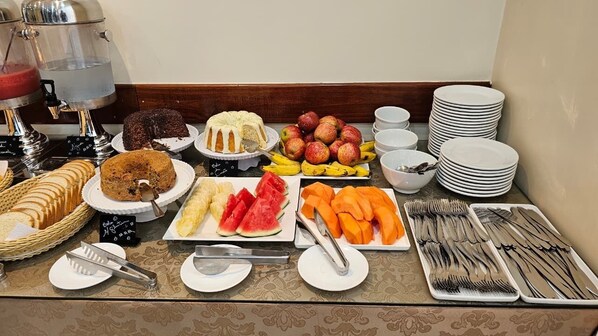 Uma mesa de buffet com diversos alimentos, incluindo bolos, frutas e utensílios.