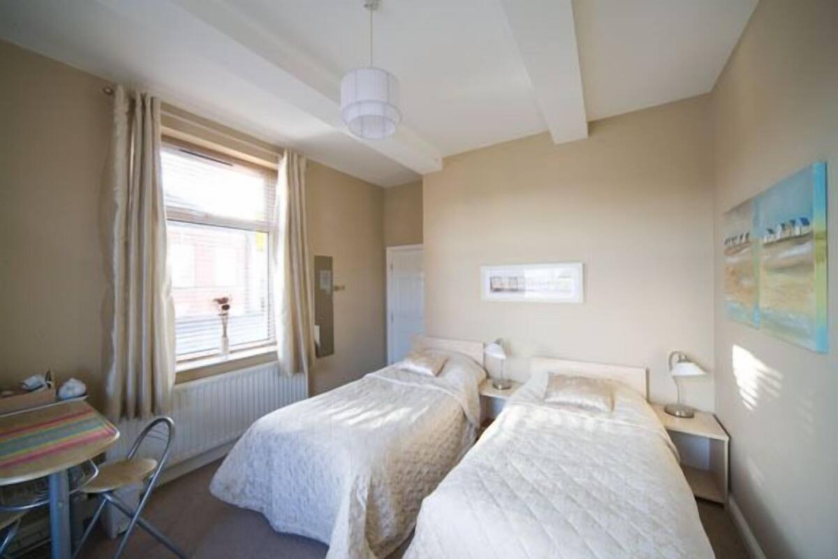 Quarto com duas camas, uma escrivaninha e janela com cortinas.