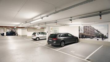 Garagem de estacionamento com vários espaços, uma carrinha branca e um carro cinzento estacionados.