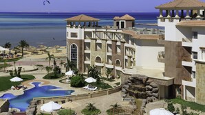 Um resort com piscina, palmeiras e vista para o oceano.