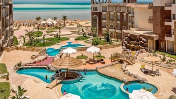 Um resort com várias piscinas, palmeiras e vista para a praia.